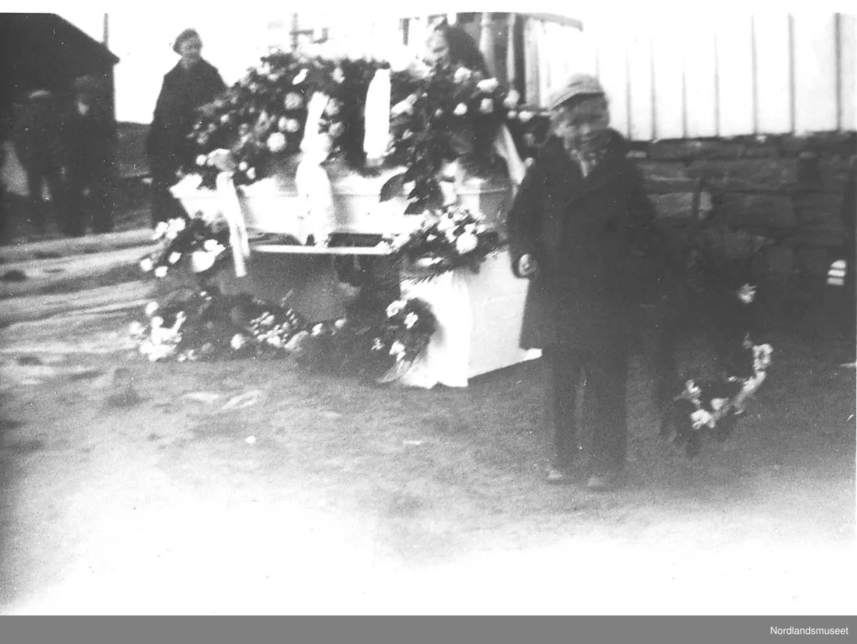 Begravelse på Inndyr, Gildeskål. Hvit kiste. Blomster. Liten gutt står ...