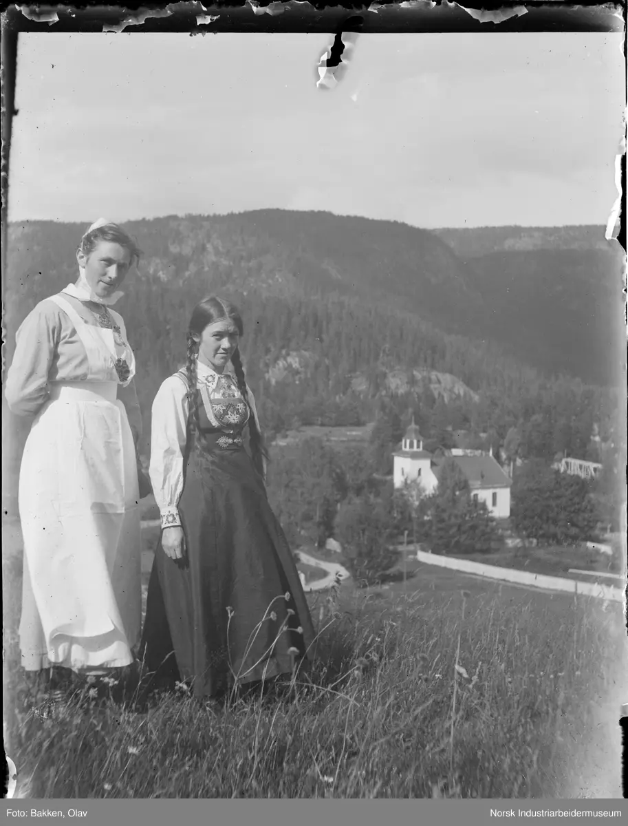 To kvinner stående på gressbakke. Gransherad Kirke i bakgrunnen ...