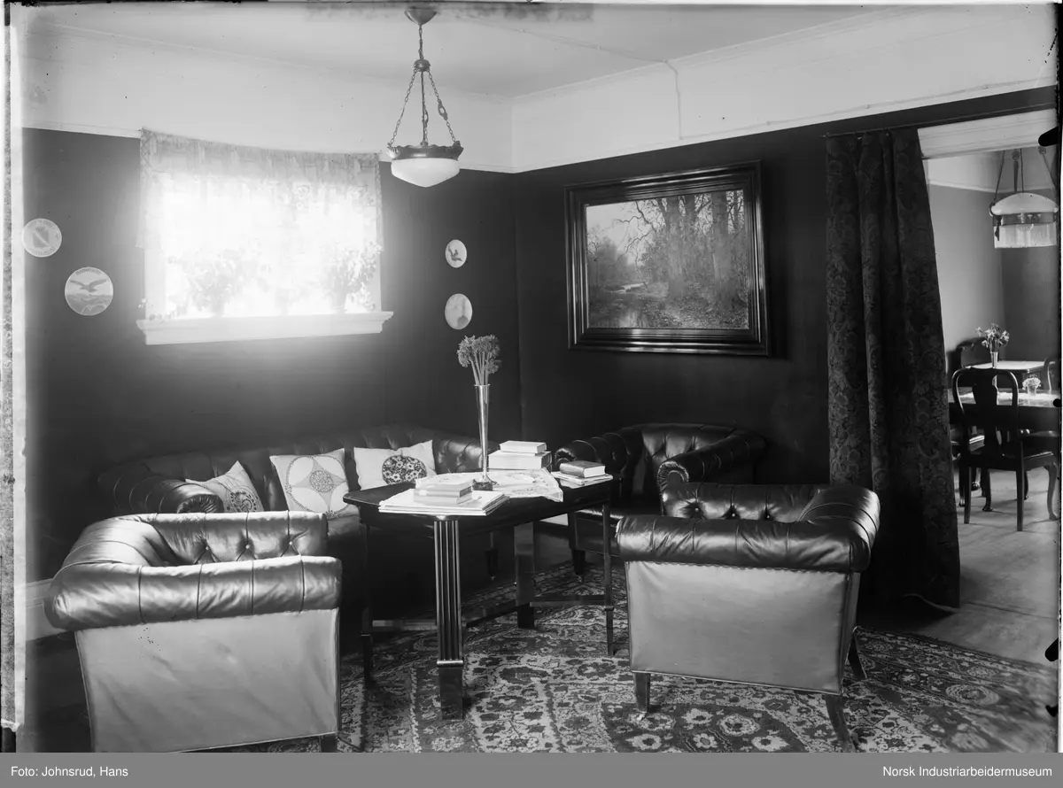 Interiør av stue. Tre stoler og en sofa med skinntrekk rundt et bord ...