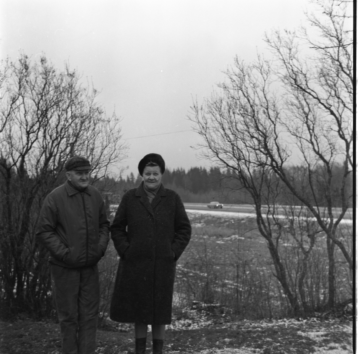 En vinterklädd äldre kvinna och man med en motorvägen bakom sig. Det ...