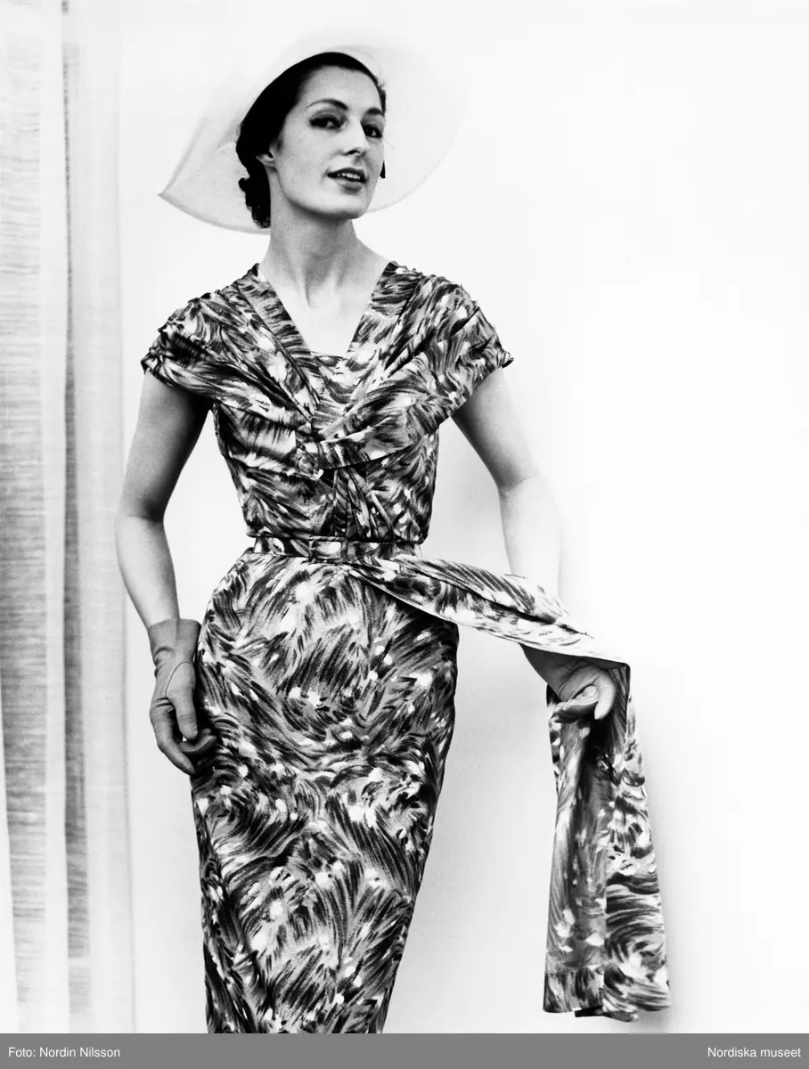 Modell i mönstrad klänning i helsiden, vit hatt och ljusa handskar ...