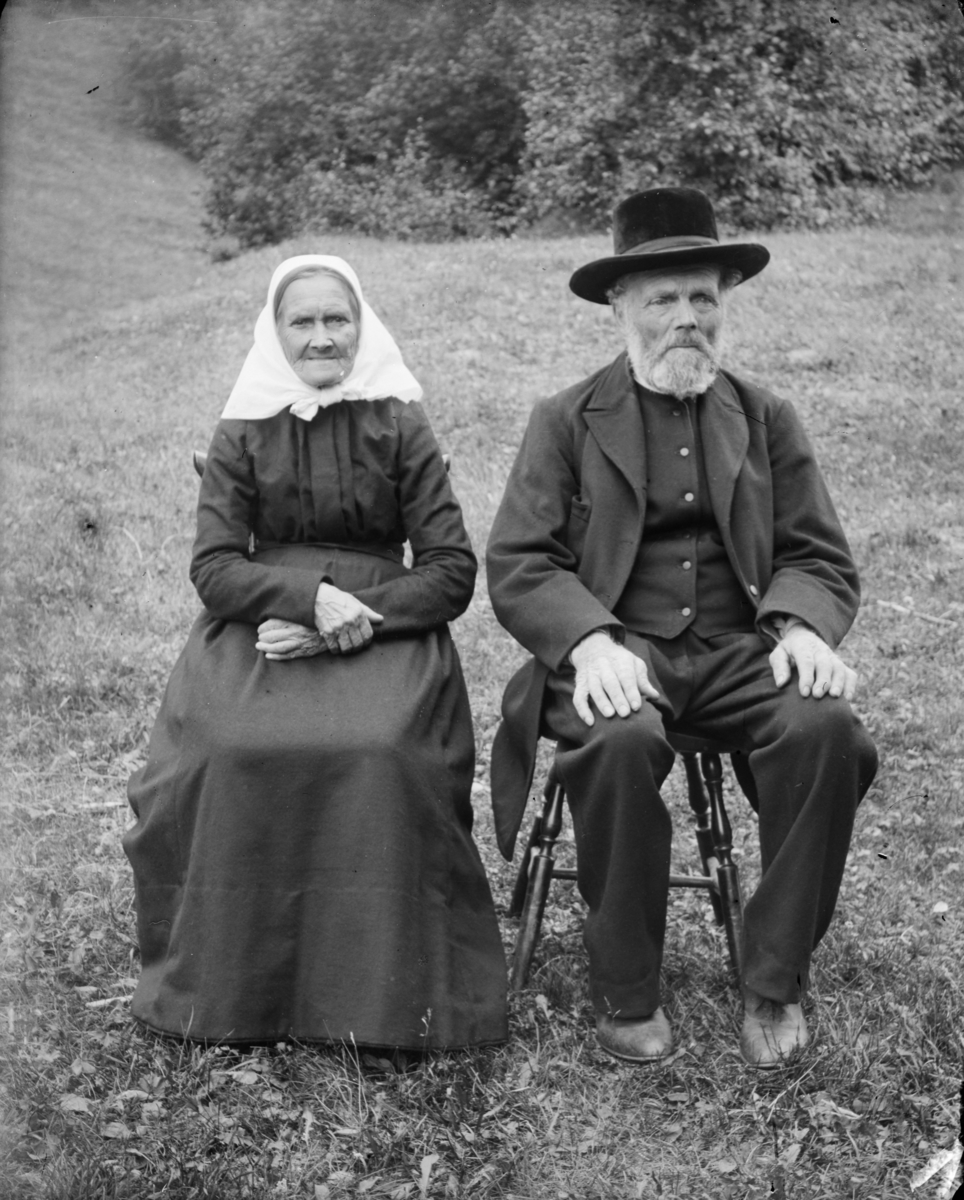 Portrett av et eldre par tatt utendørs. Hun med skaut og han med hatt ...