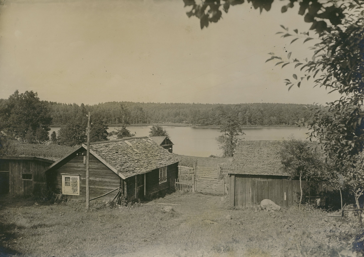 Småhus vid fägatan. Till vänster en gammal stuga. Till höger en lada ...