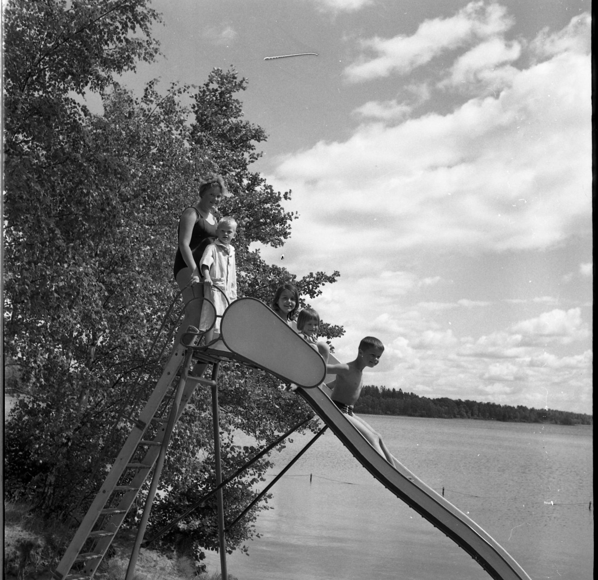 Fem barn i olika åldrar sitter i en rutschkana vid en badstrand ...