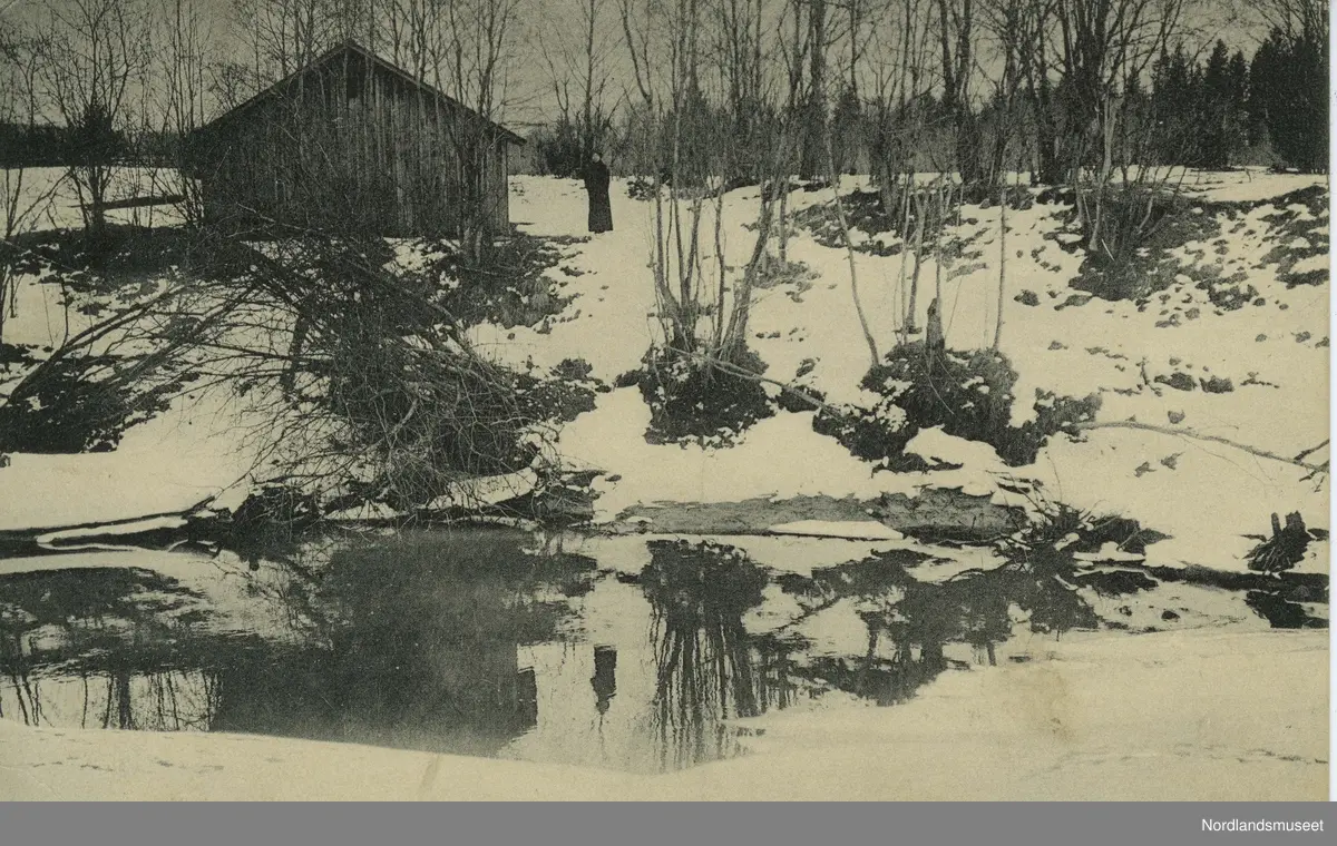 Postkort med bilde av vinterlandskap. Liten dam midt på bildet, bygning ...